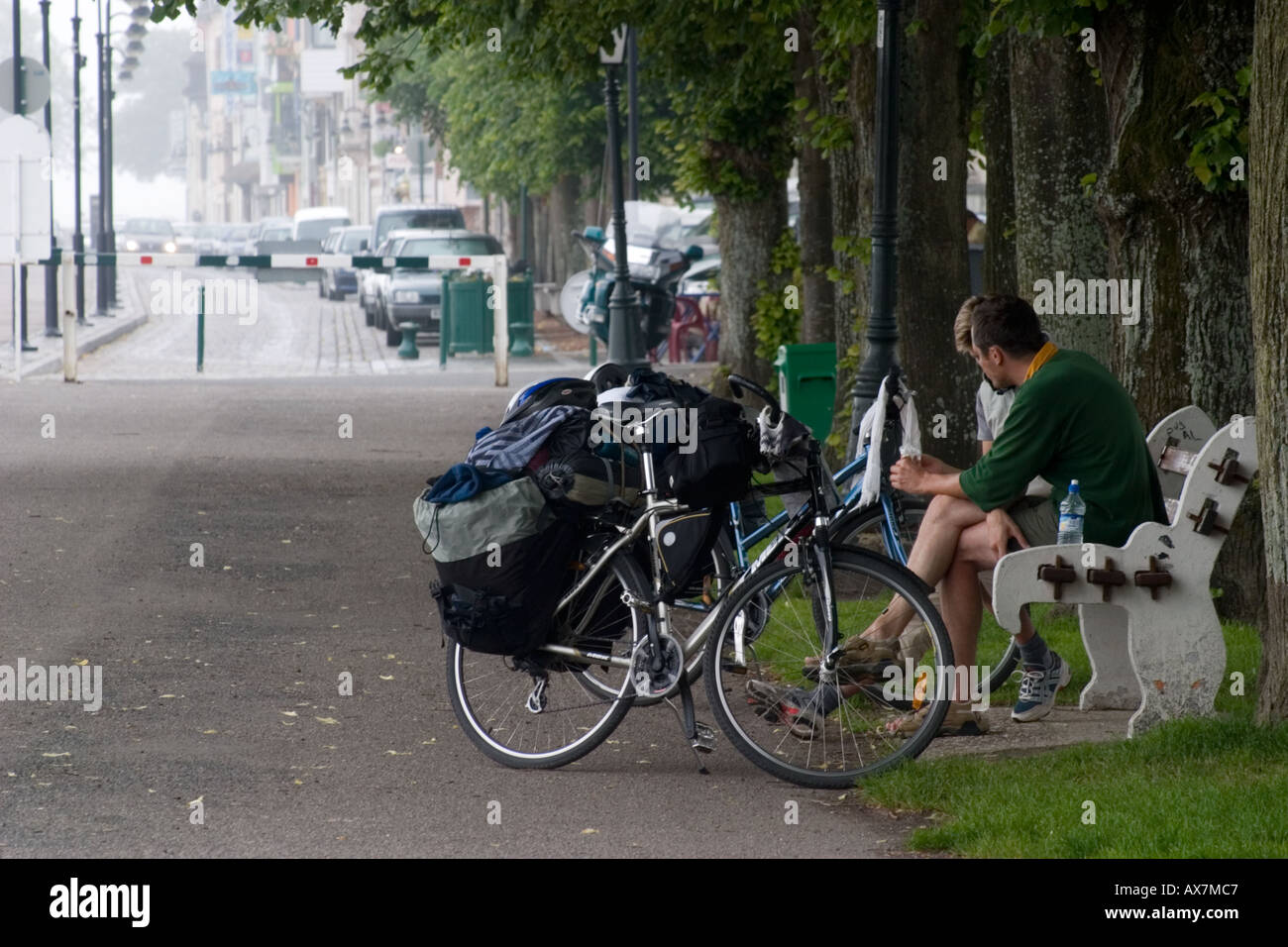 Couple of cyclists take a break and rest on a bench on the riverside ...