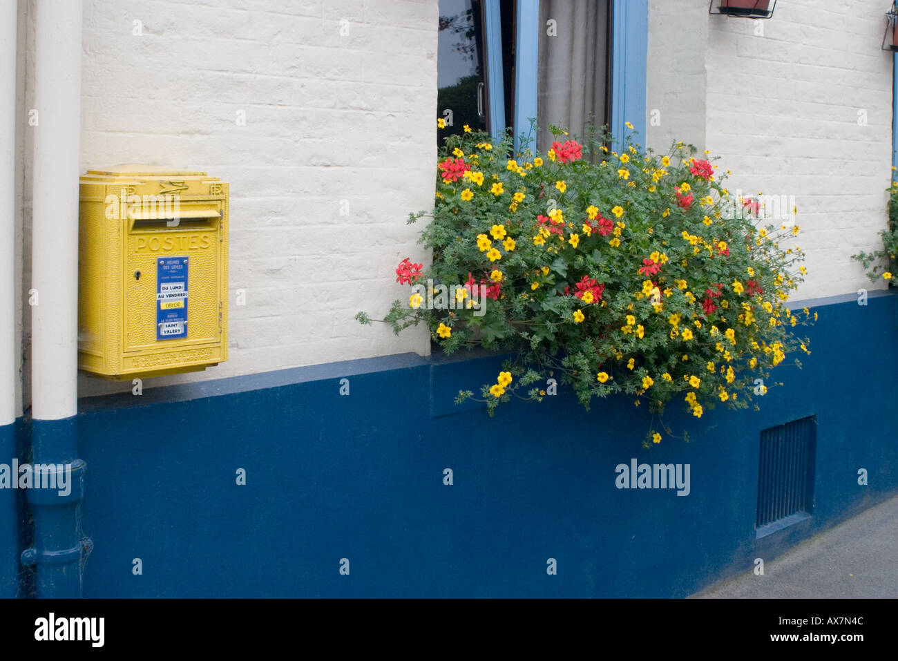 Yellow French post post on blue wall of cottage with flowers on window ...