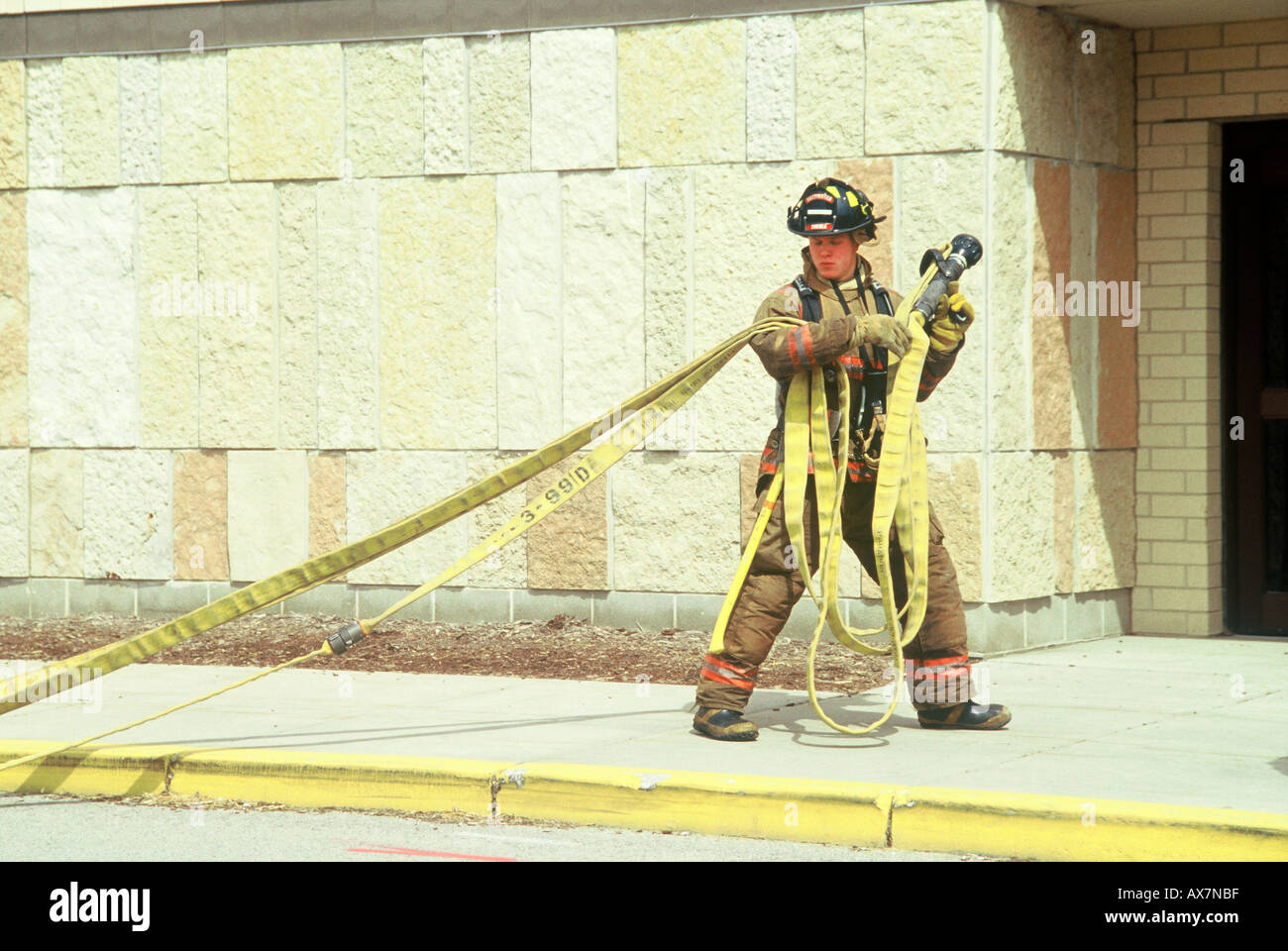 A fire fighter is holding the fire hose over his shoulder ready to ...