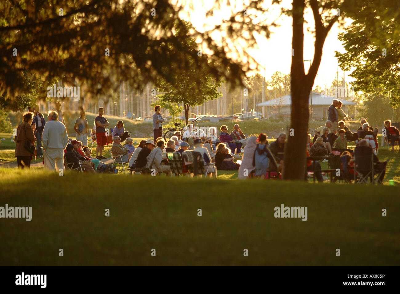 A large group of people gather at a park in the evening to watch a ...