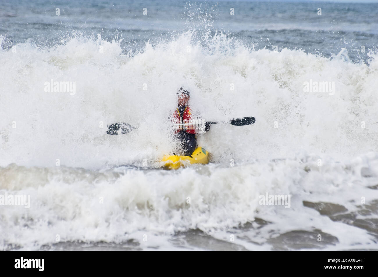 Teenage boy in a kayak wiped out in the surf and big waves on a beach ...