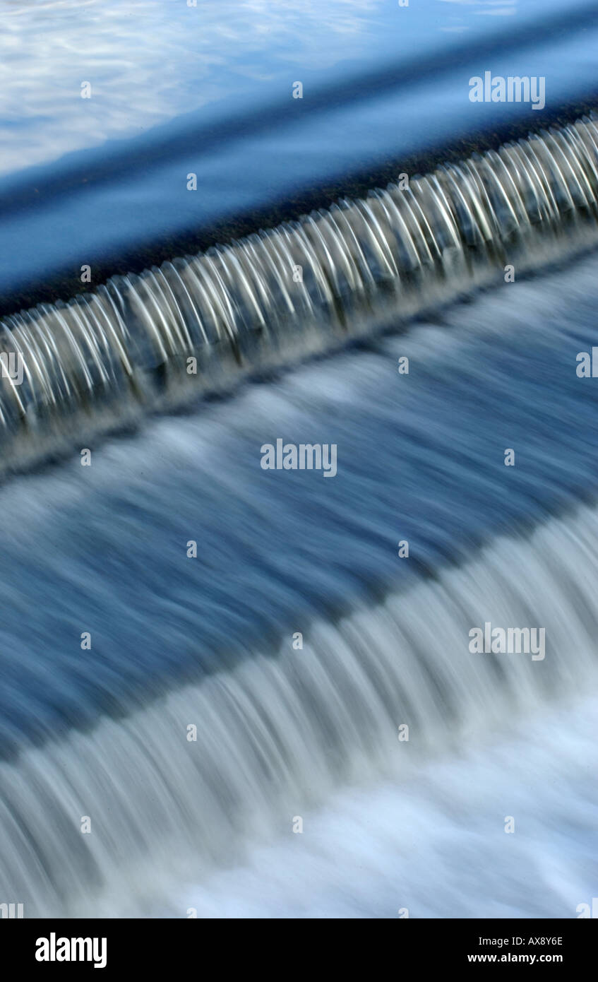 Smooth flowing water over a wear. Dappled blue light glinting off the ...