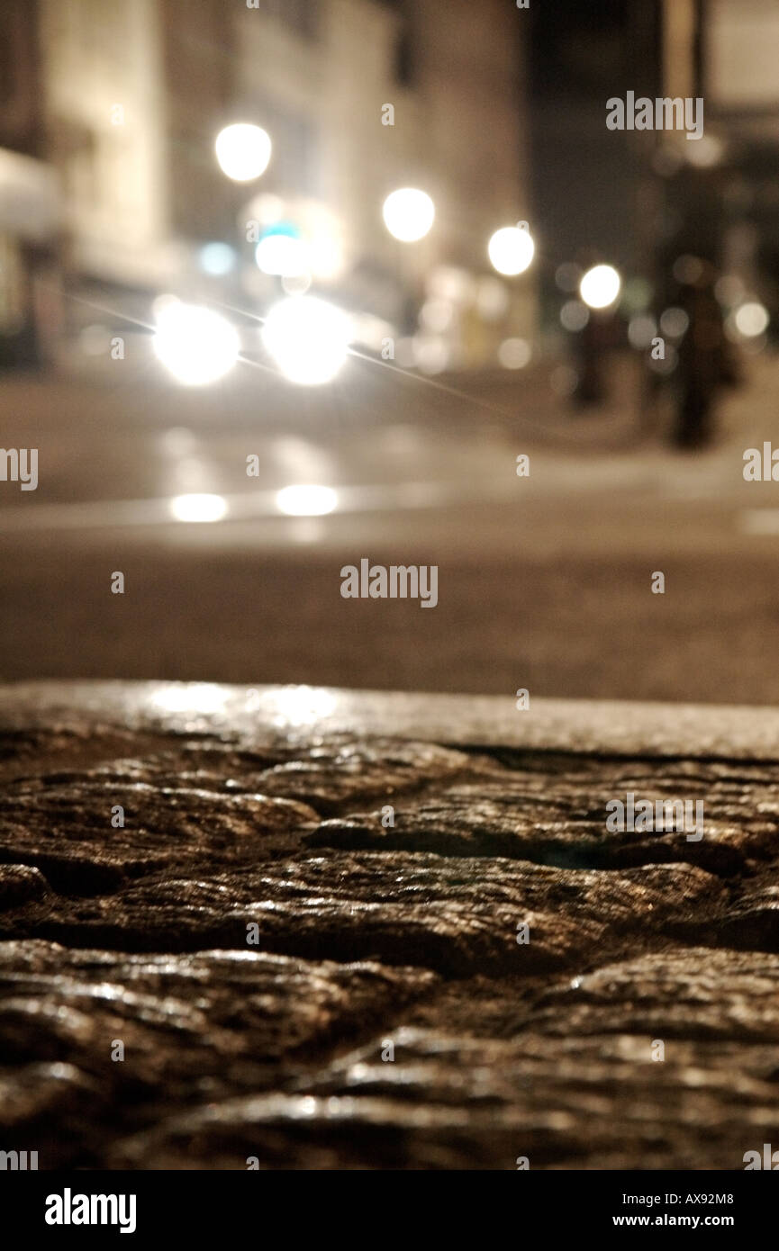 Night scene taken from pavement level with car headlights in background ...