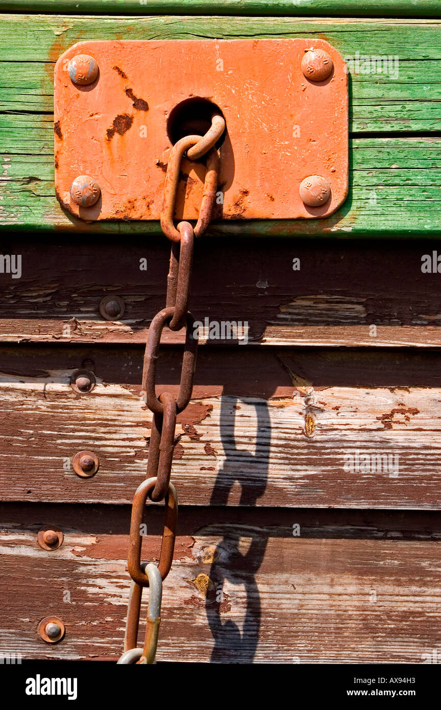 Rusty chain coming out of a hole in the side Stock Photo - Alamy