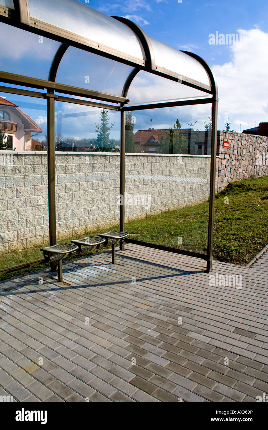A modern bus stop with a metal and glass shelter, three metal seats, a ...