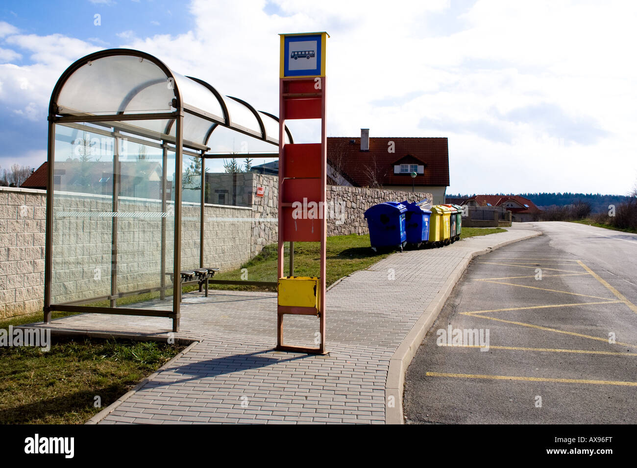 A suburban bus stop with a glass and metal shelter, a red and yellow ...