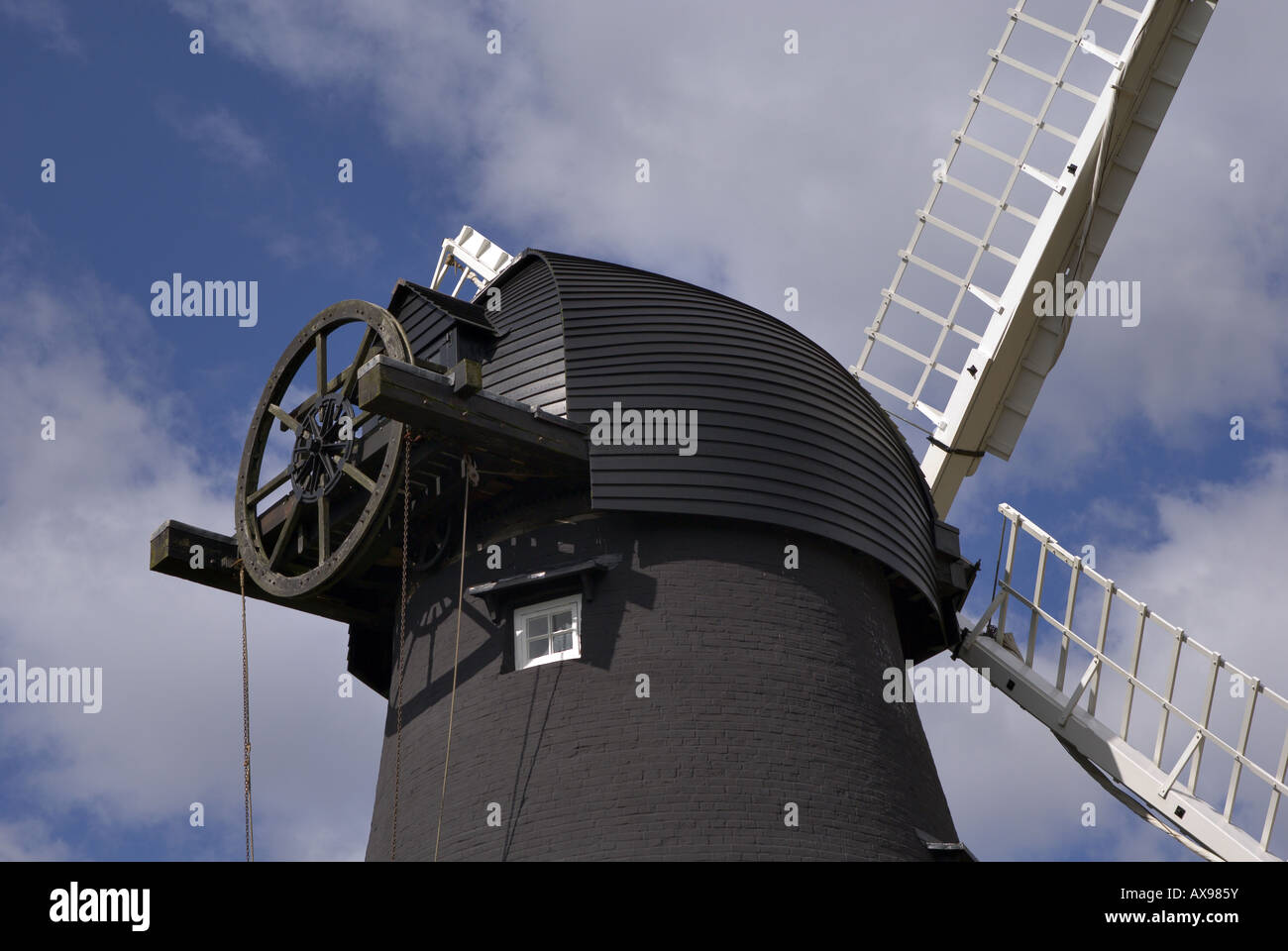 A windmill with its cap turning wheel and open sails against a blue sky ...