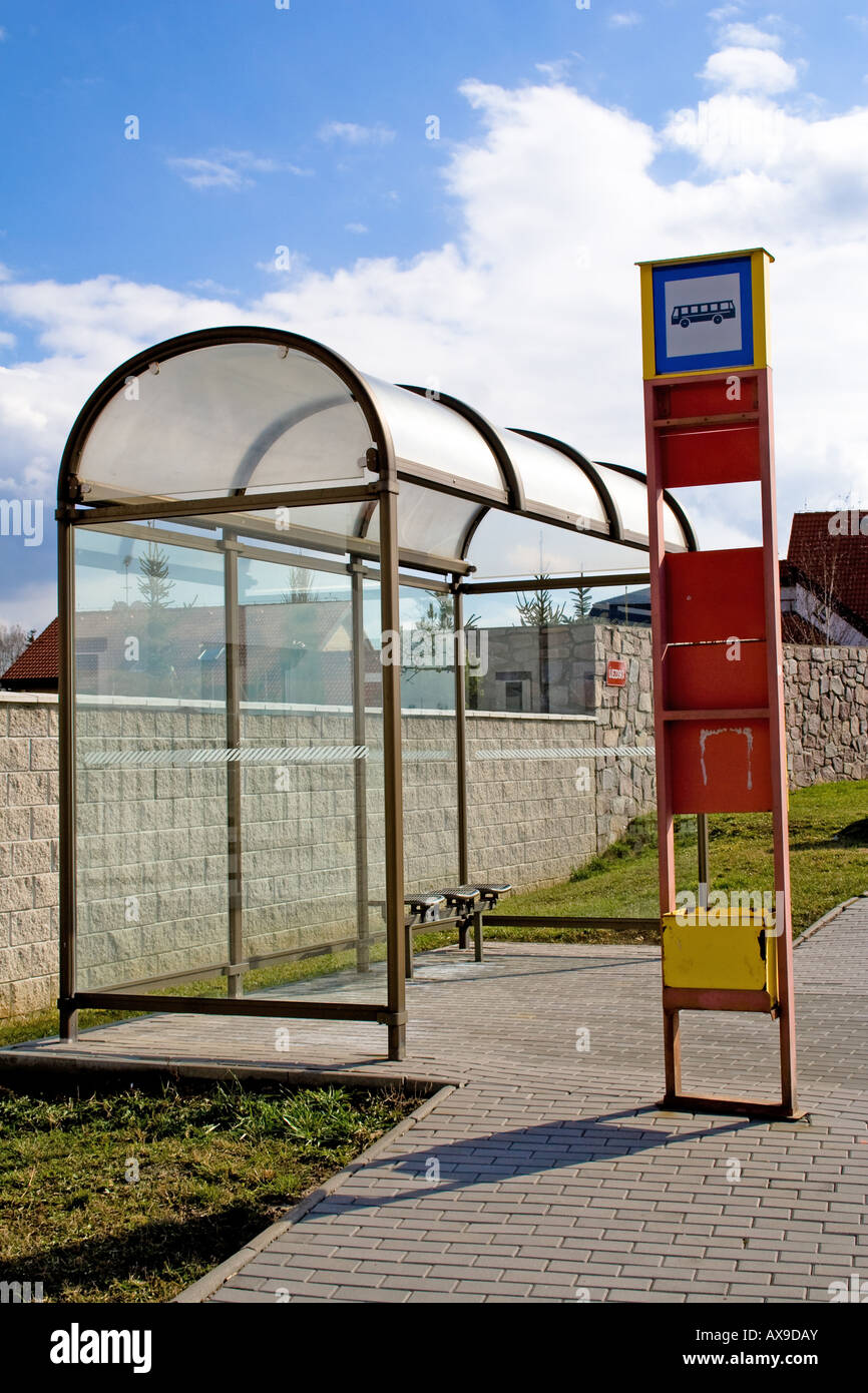 A suburban bus stop with a modern glass and metal shelter, a red and ...