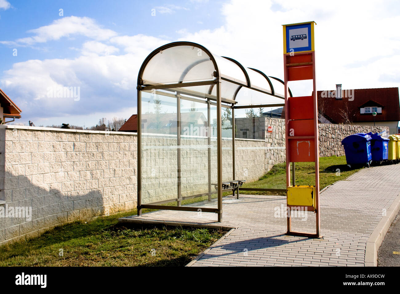 A suburban bus stop with a glass and metal shelter, a red and yellow ...