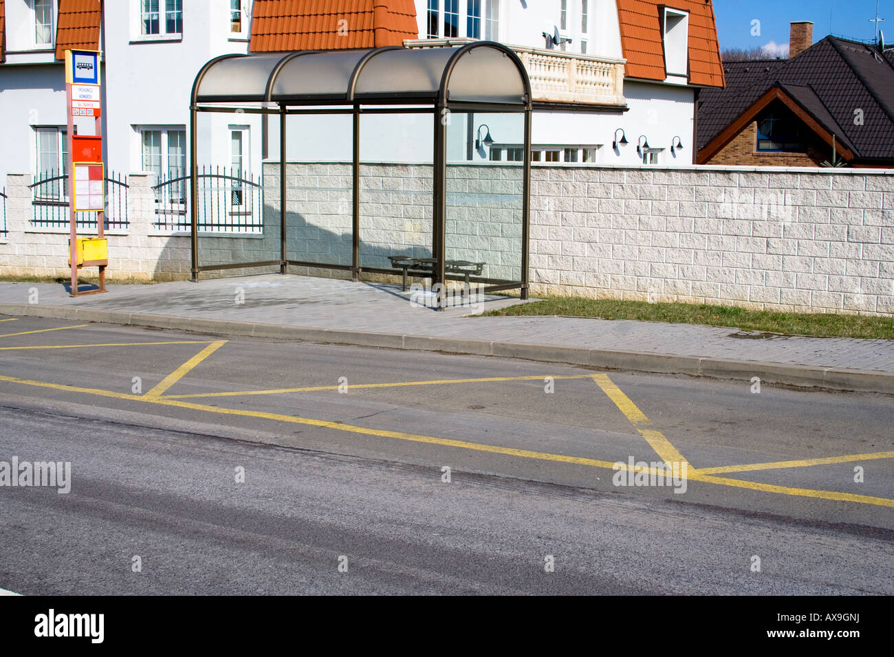 A suburban bus stop with a glass and metal shelter, a red and yellow ...