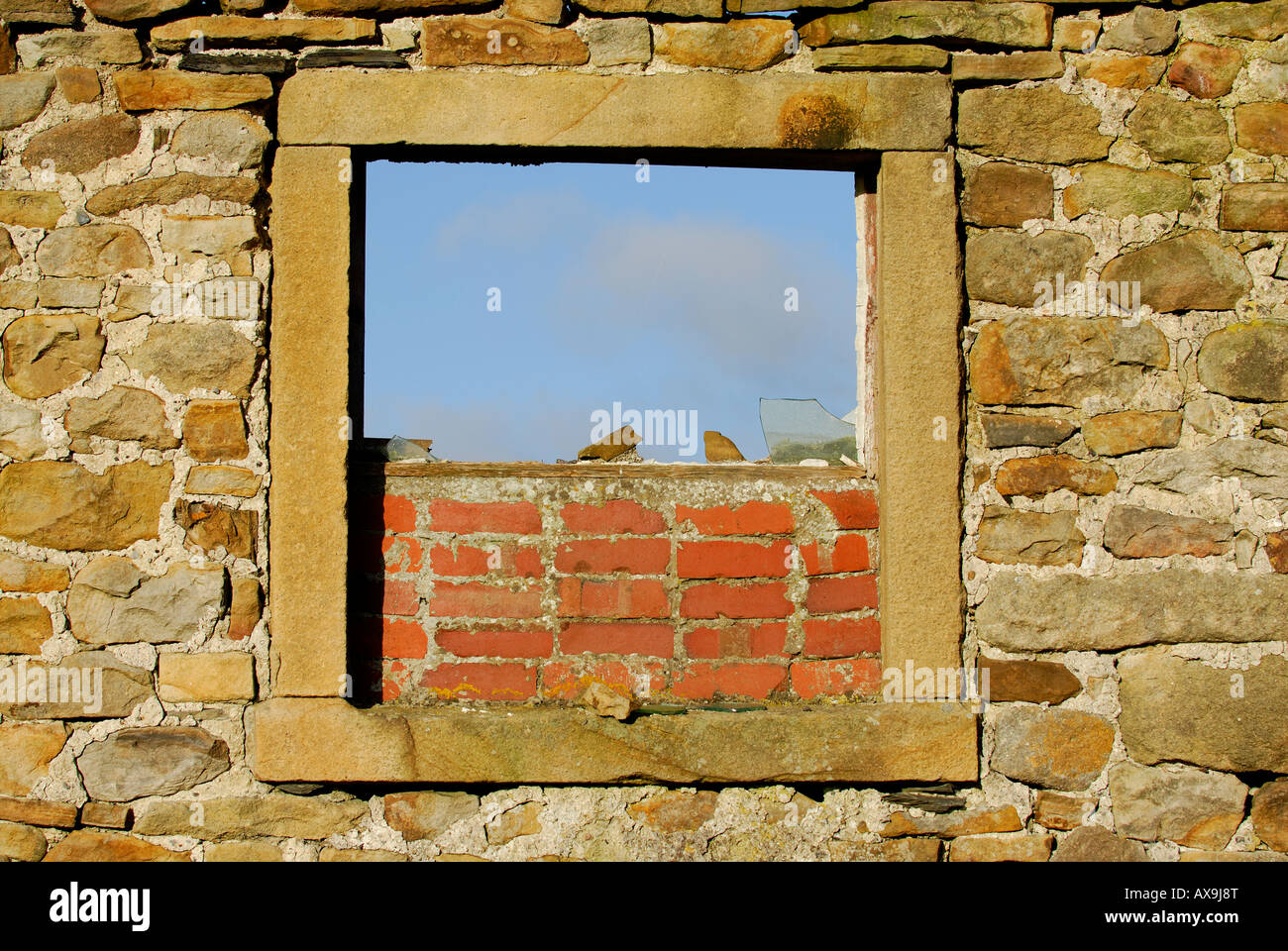A stone wall with a window frame shows the sky, with broken glass and ...