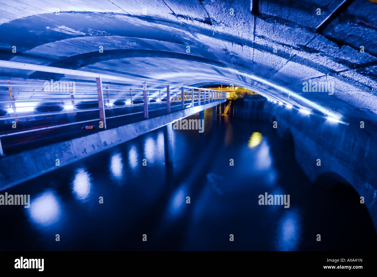 A blue-lit tunnel with a bridge over water Stock Photo - Alamy