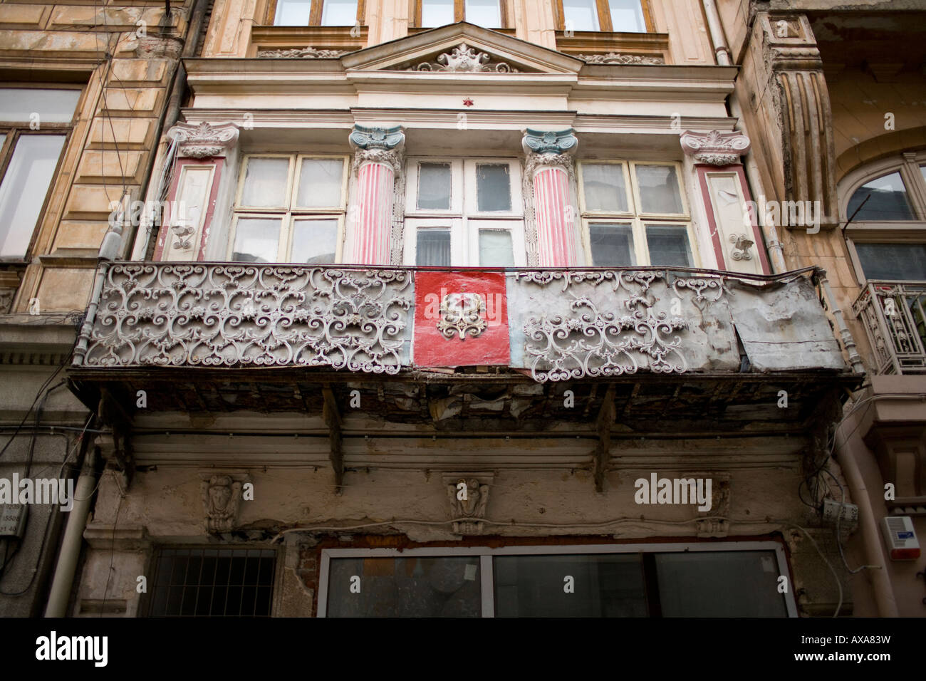 front part of on old building with a red flag hanged on the banister of ...