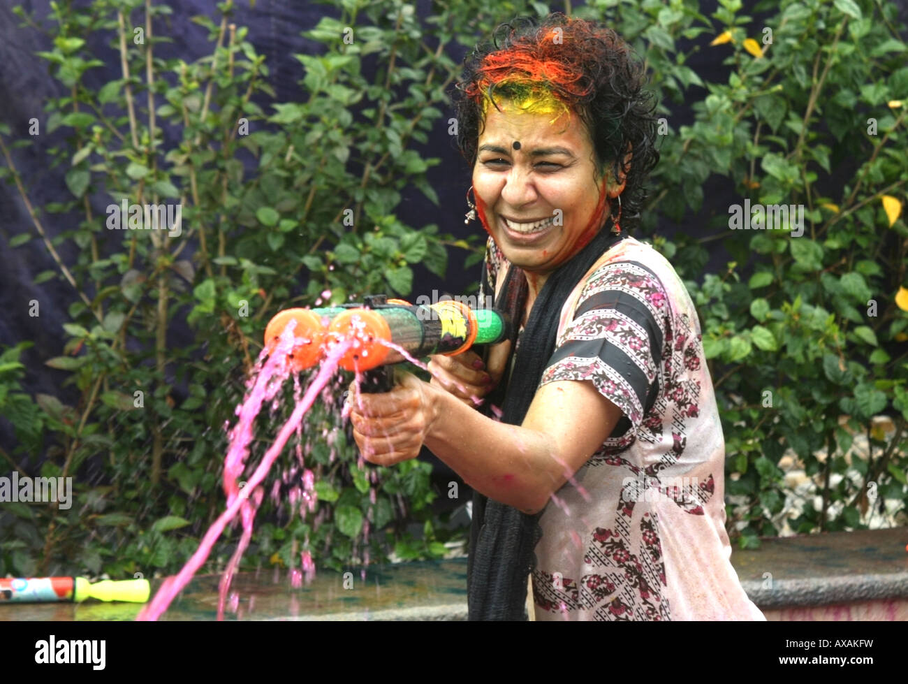 Woman covered in holi powder spraying a watergun at the Indian spring ...