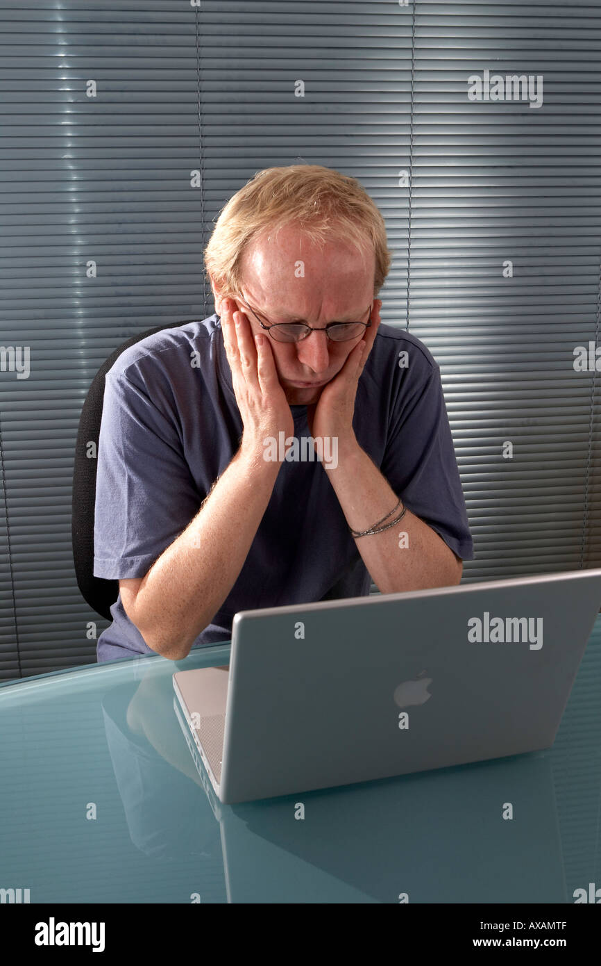 Casually dressed man sitting stressed at computer with his head in his ...