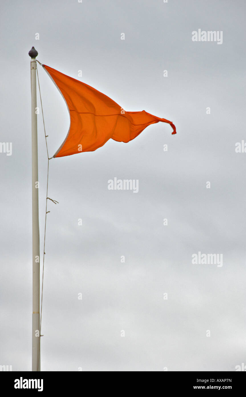 A orange warning flag flying in the wind in grey sky Stock Photo - Alamy