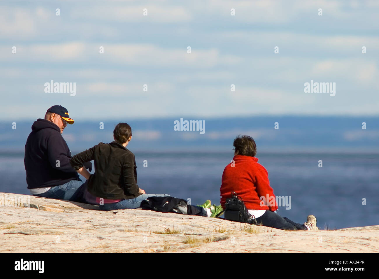 Three tourists sitting on a rock observing nature at Tadoussac Stock ...