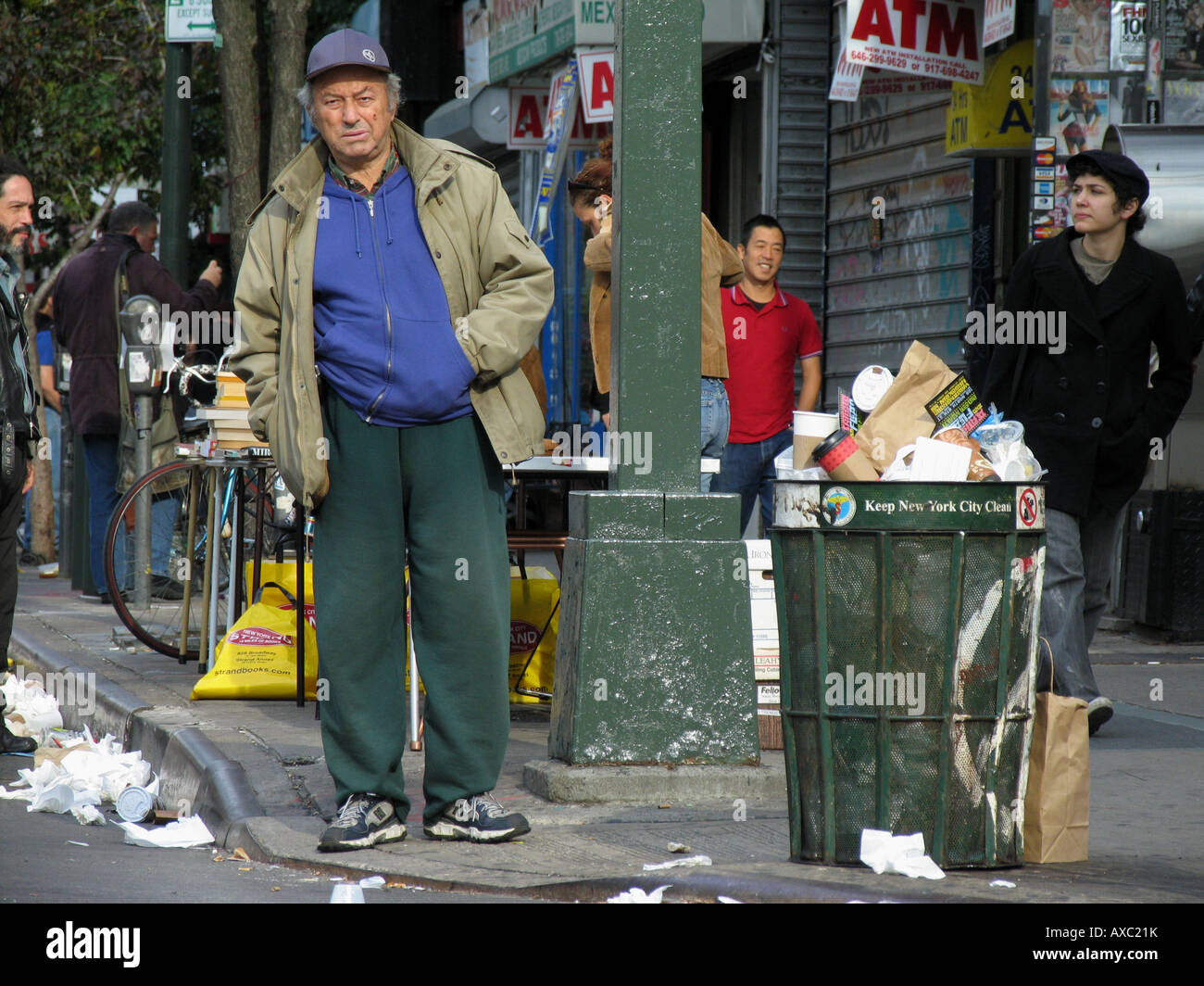 older man next to a dustbin at a dirty street is looking into the ...