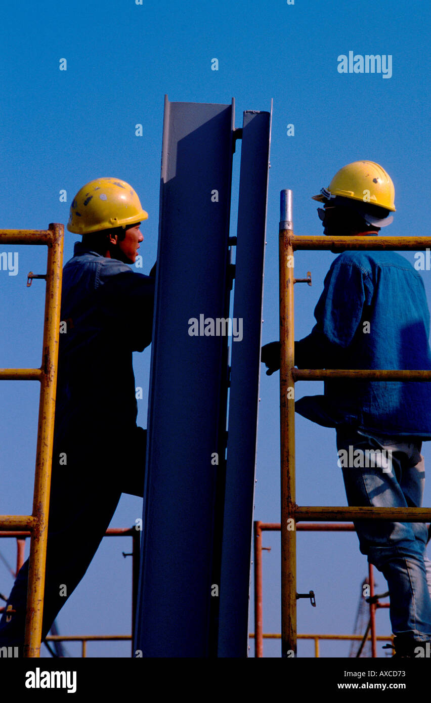 Two construction workers stand on scaffolding on either side of a ...