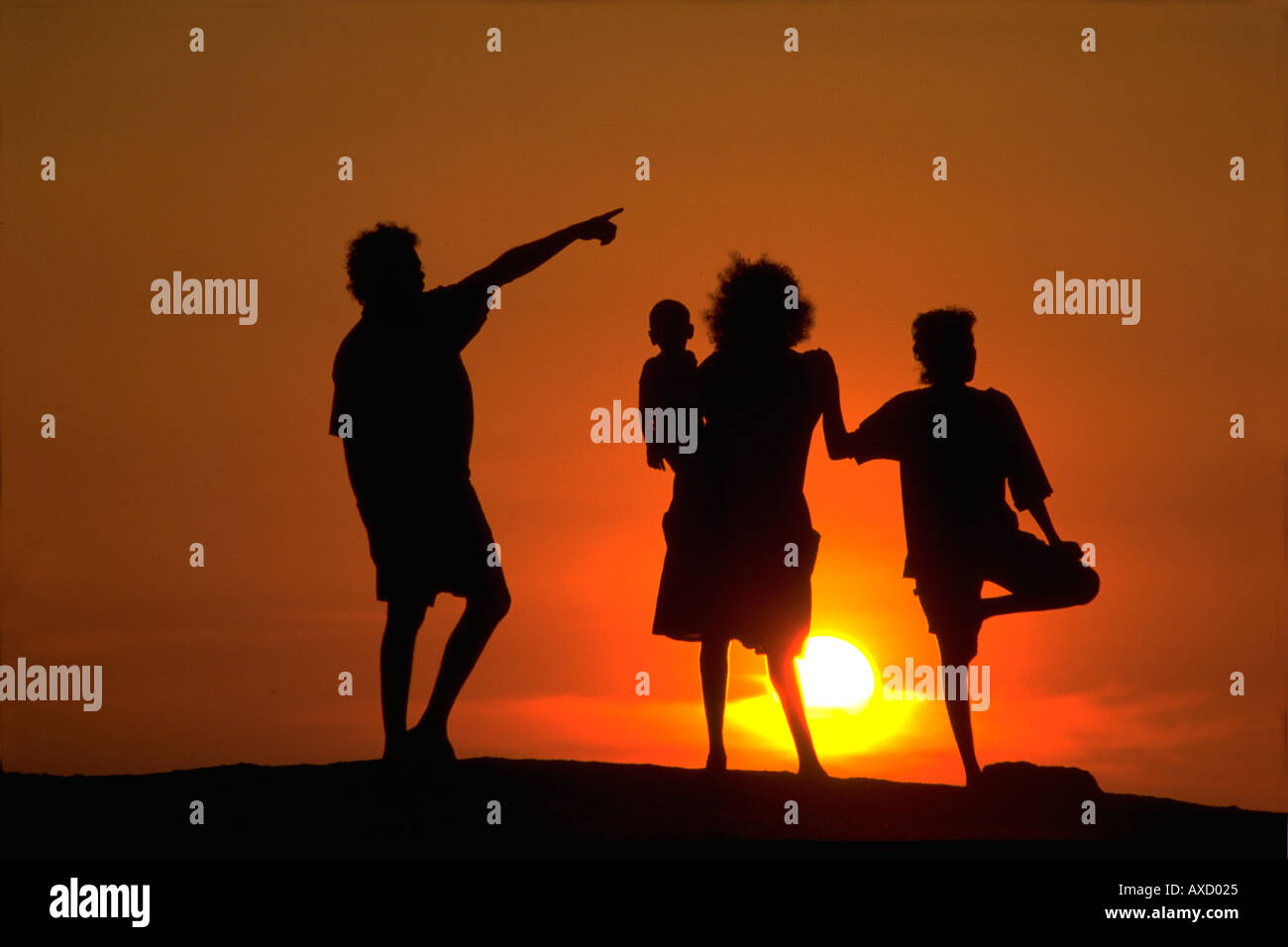 Aboriginal family silhouetted against setting sun on clifftop at sunset ...