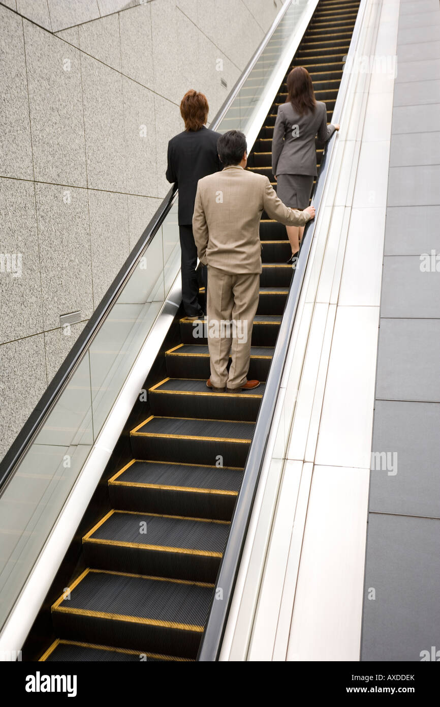 Three business people ascending escalator Stock Photo - Alamy