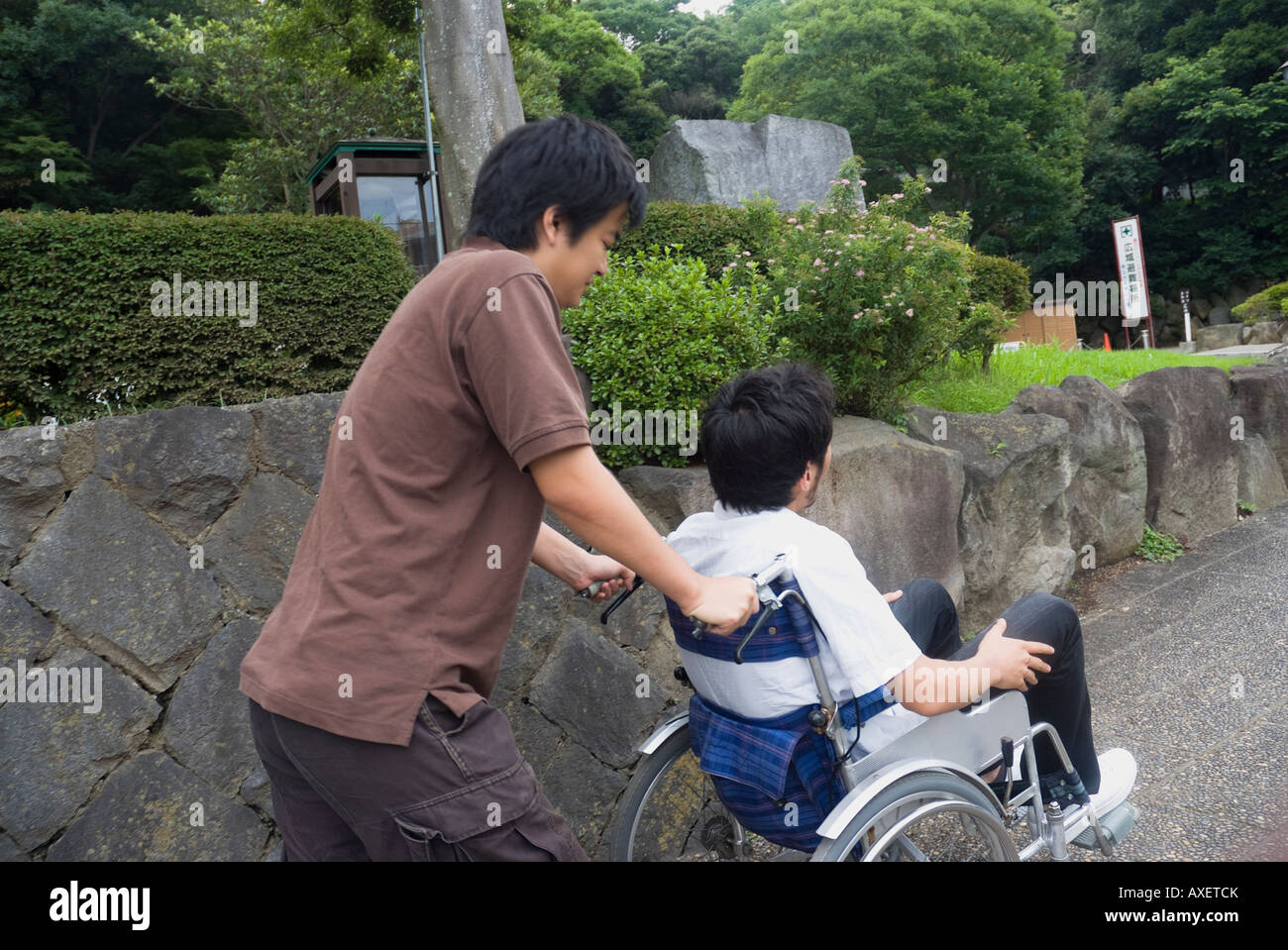 Young man pushing man on wheelchair Stock Photo - Alamy