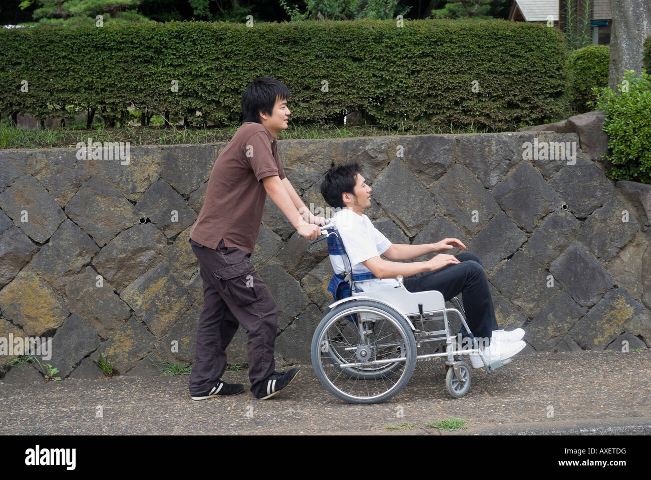 Young man pushing man on wheelchair Stock Photo - Alamy