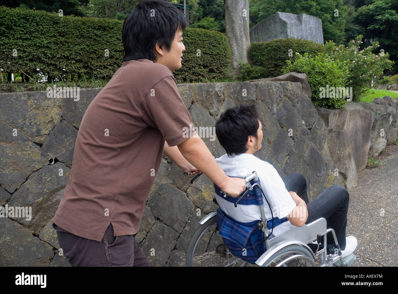 Young man pushing man on wheelchair Stock Photo - Alamy