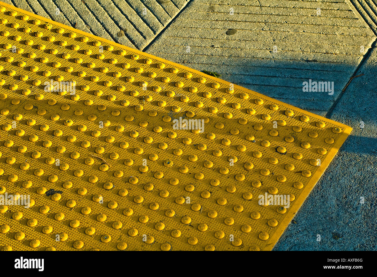 Yellow textured handicap pad on sidewalk with the sun shining across it ...