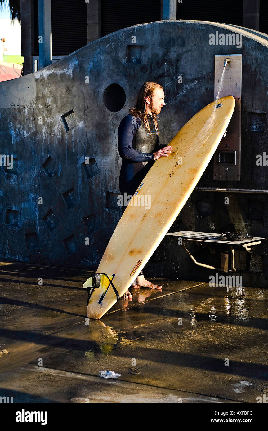 Surfer in black wet suit washes his surf board off under an outdoor ...