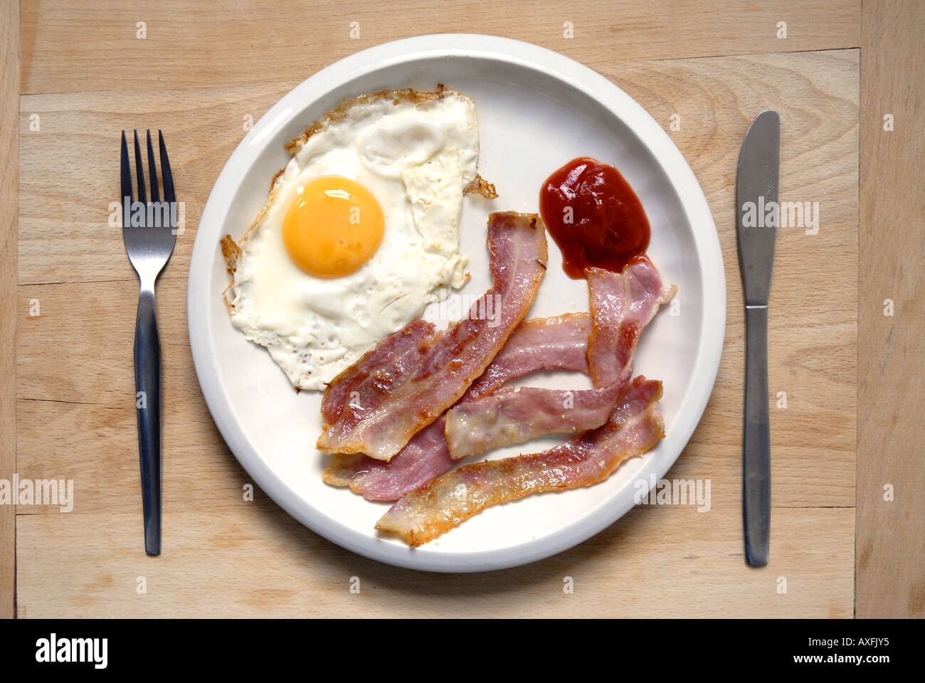 A fried egg and two rashers of streaky bacon with tomato ketchup on a ...