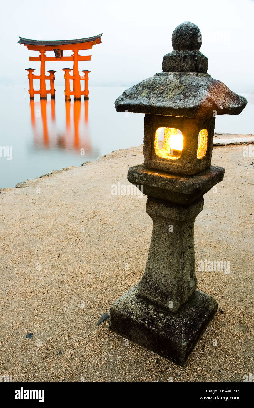 A stone lantern stands in front of the floating torii gate of Miyajima ...