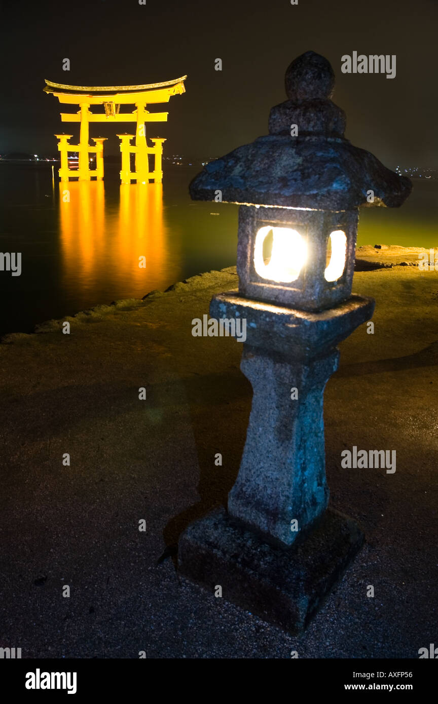 A stone lantern stands in front of the floating torii gate of Miyajima ...
