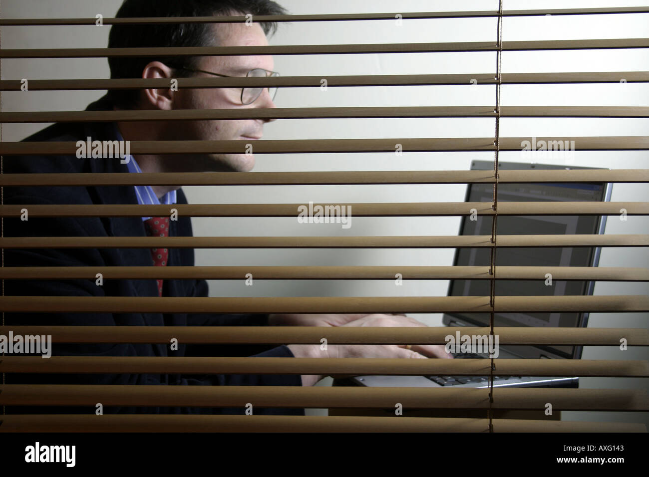 Business man in his office behind blinds on his notebook computer with ...
