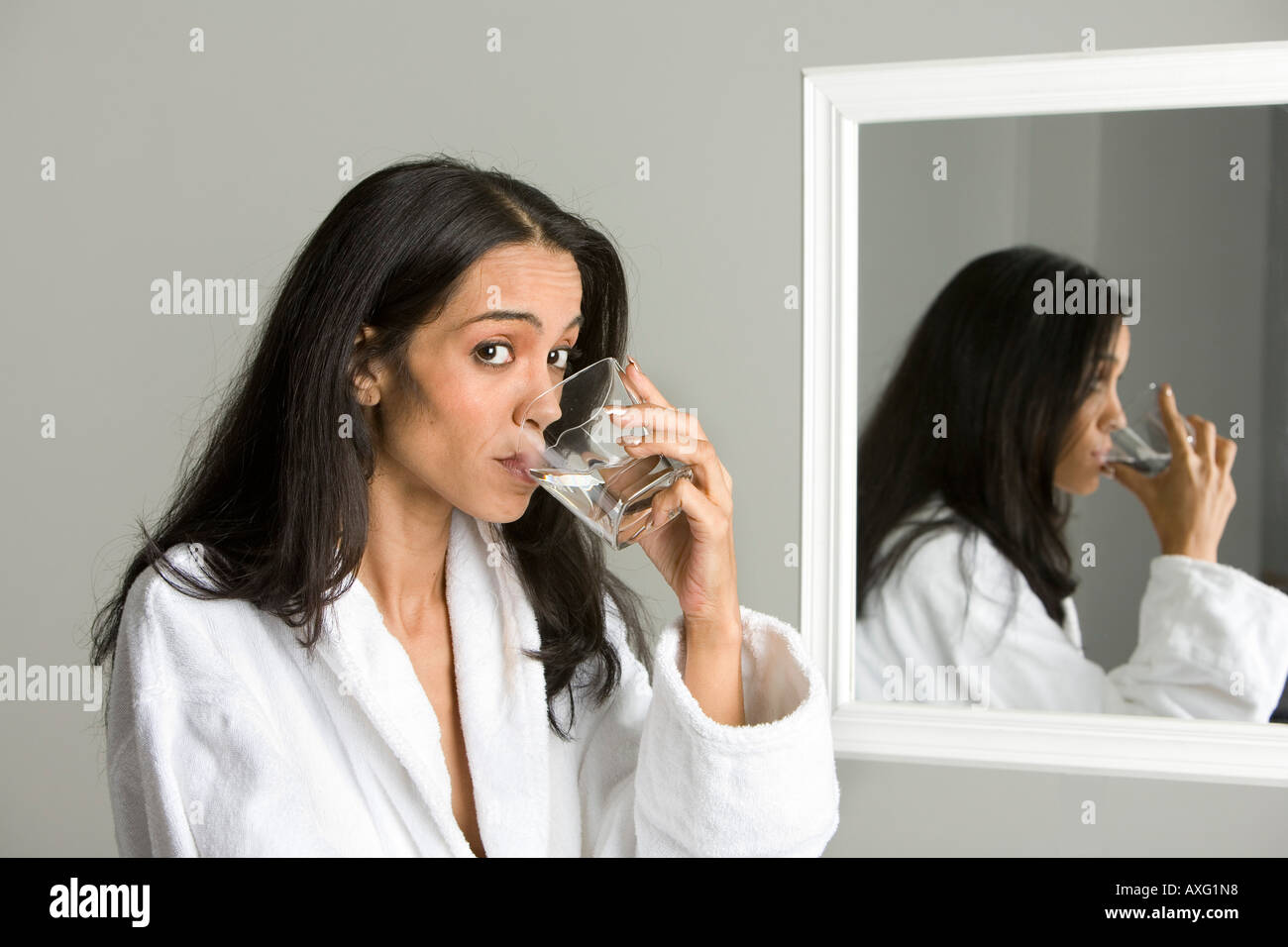 An attractive young woman drinking water before her reflection in a ...