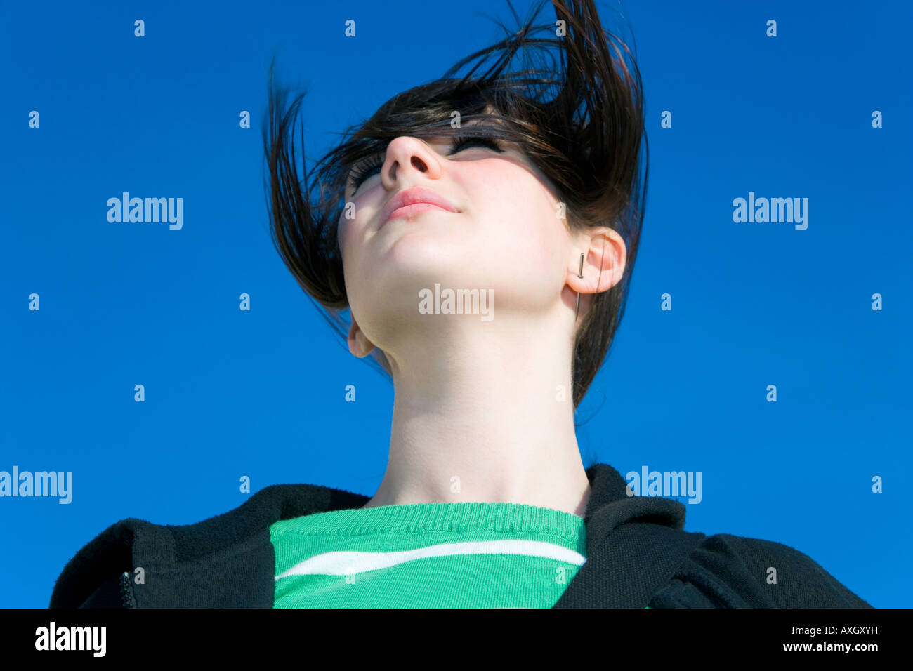 Low perspective outdoors portrait of a young girl with windswept hair ...