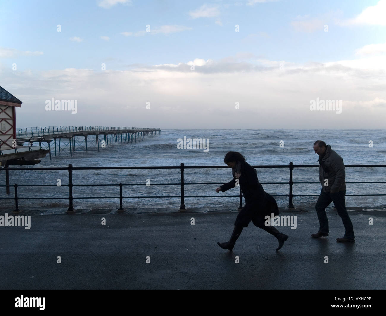 Man and woman in severe bad weather walking on promenade against a gale ...