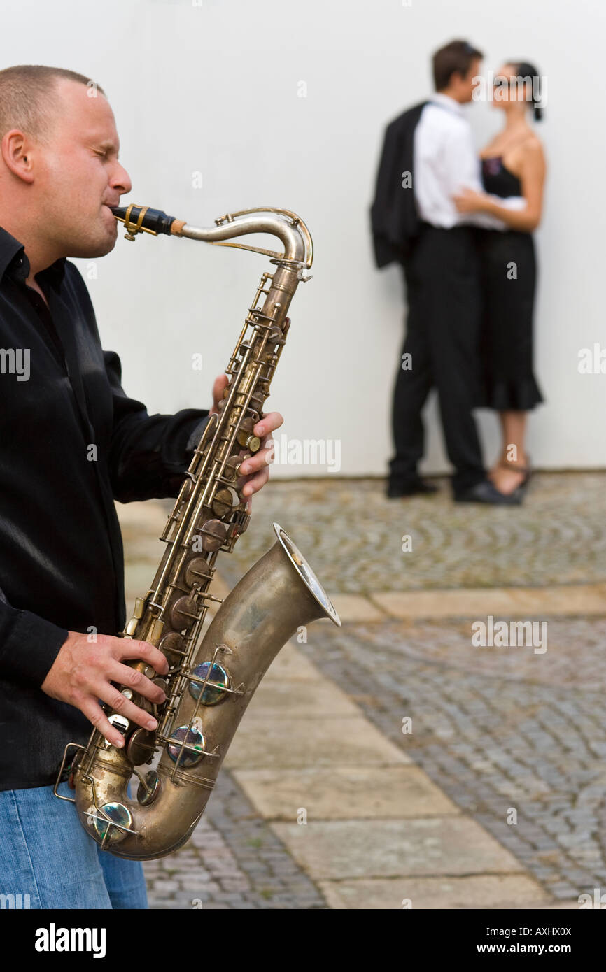A street musician playing his saxophone serenades two young lovers ...