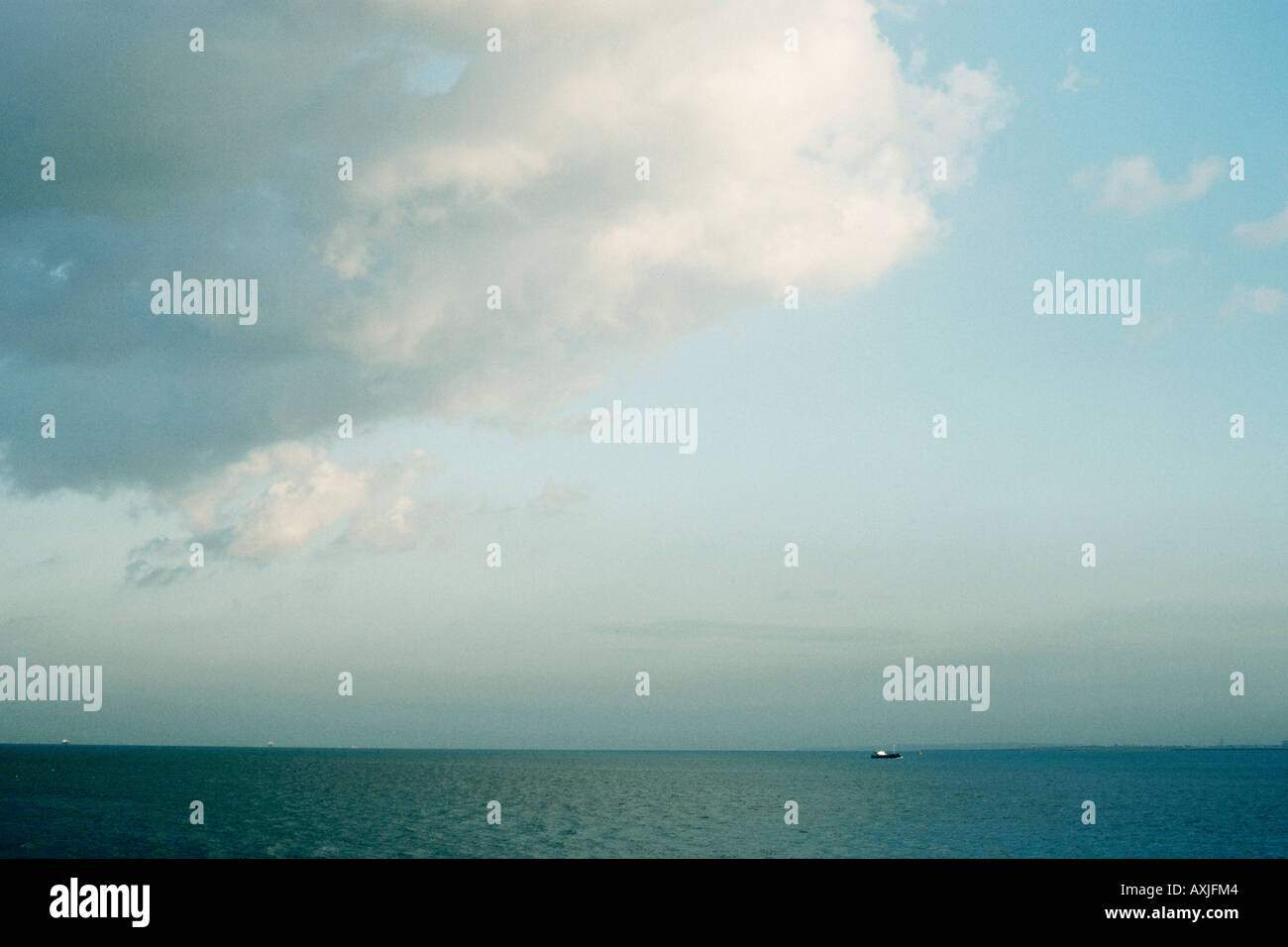 A single boat on the sea with large white cloud overhead and blue sky ...