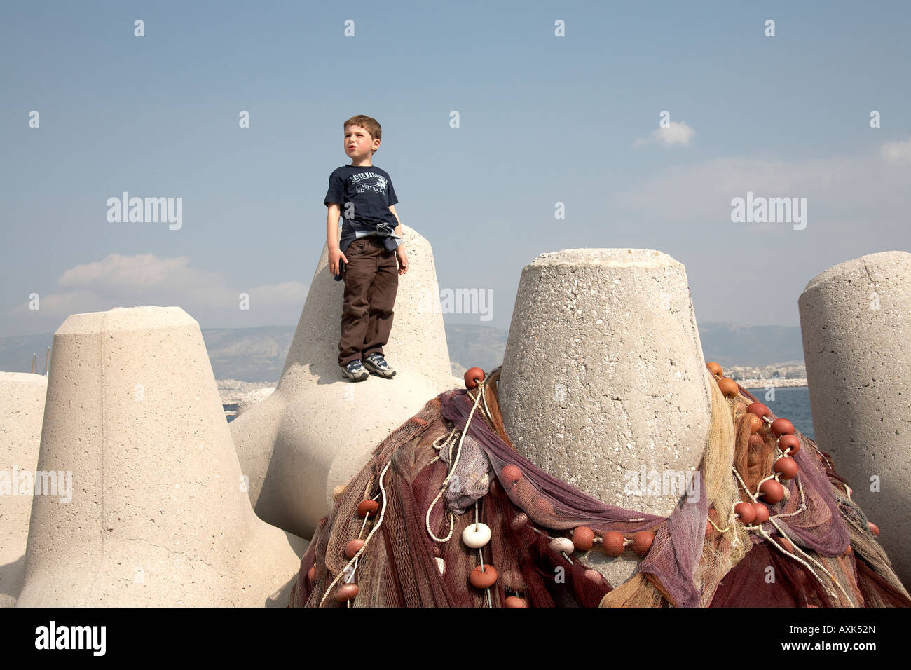 Young boy child on concrete sea wall defences with fishing nets in ...