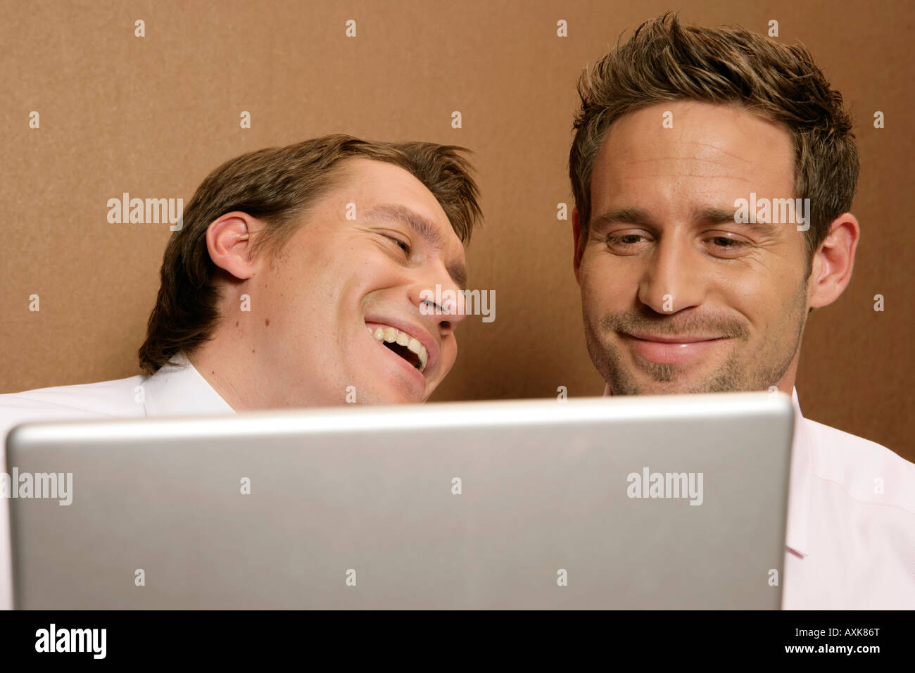 Two businessmen using laptop, both laughing Stock Photo - Alamy
