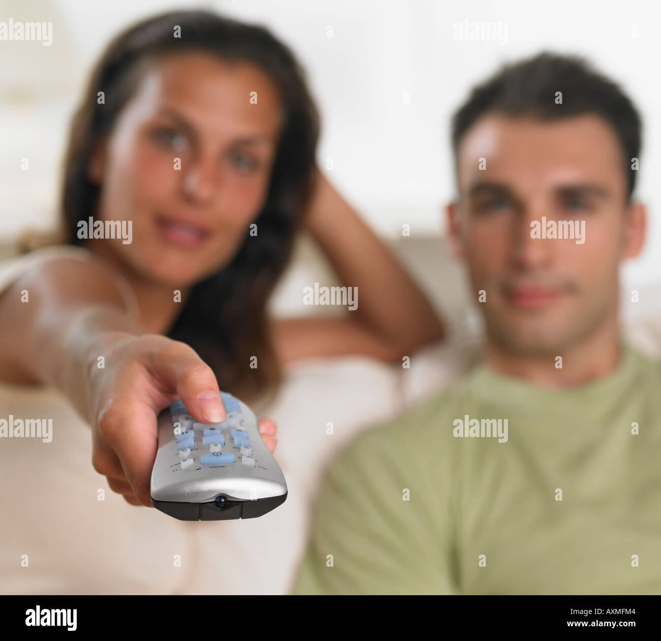 Couple sitting on sofa pointing remote control Stock Photo - Alamy