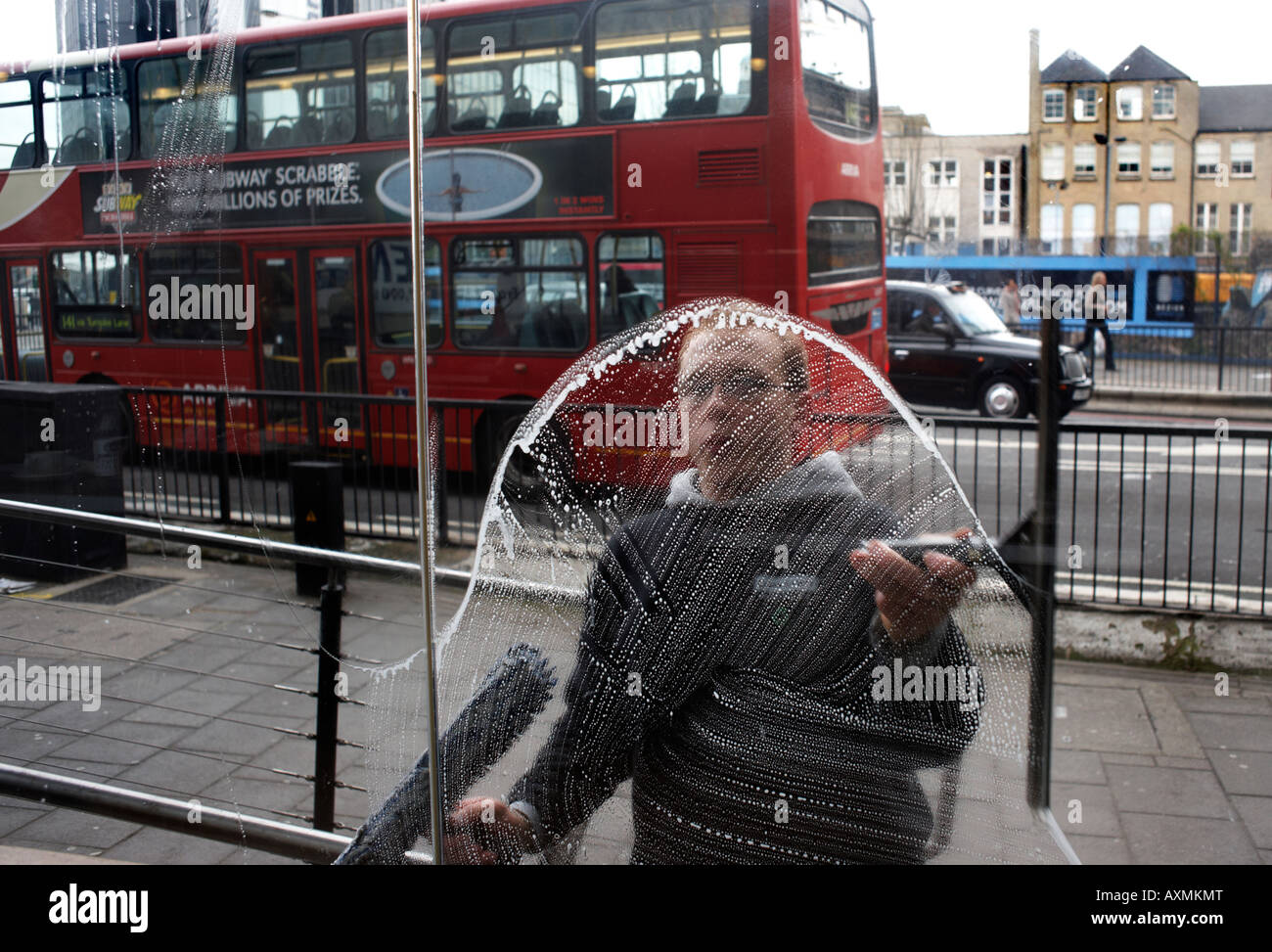 With busy traffic behind a young window cleaner wipes a circle of soapy ...