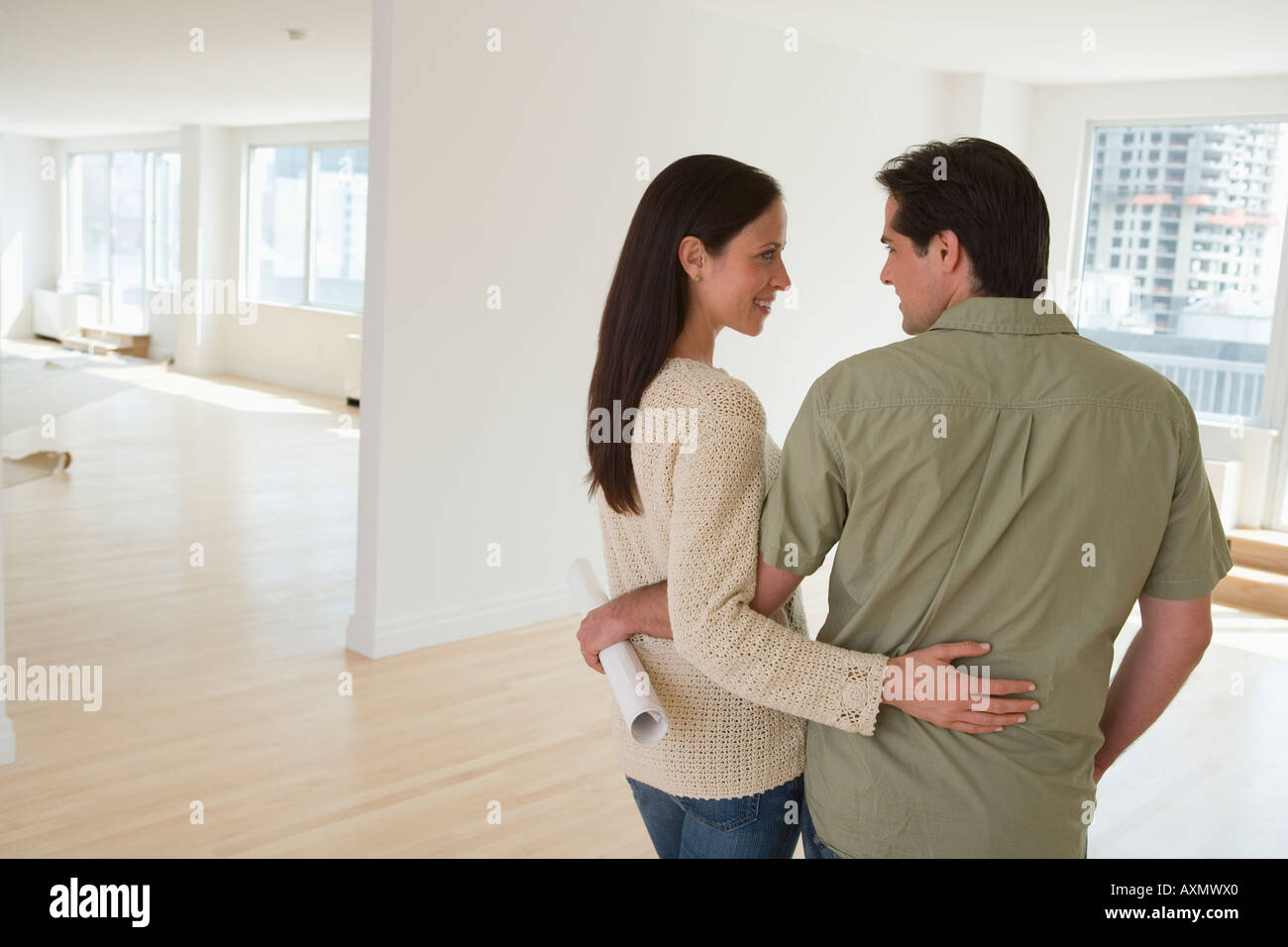 Couple hugging and holding blueprints in empty house Stock Photo - Alamy