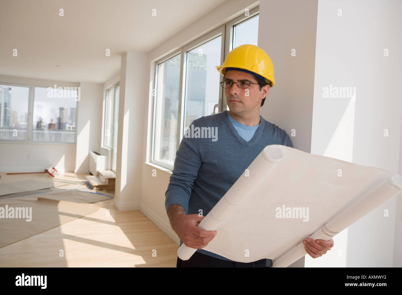 Man wearing hard hat and holding blueprints in house Stock Photo - Alamy