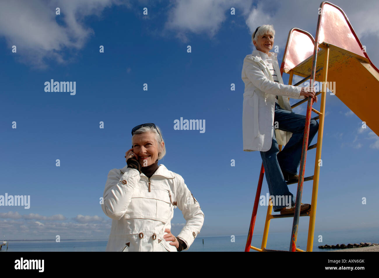 Mature woman climbing at a slide, an other woman using a mobile phone ...