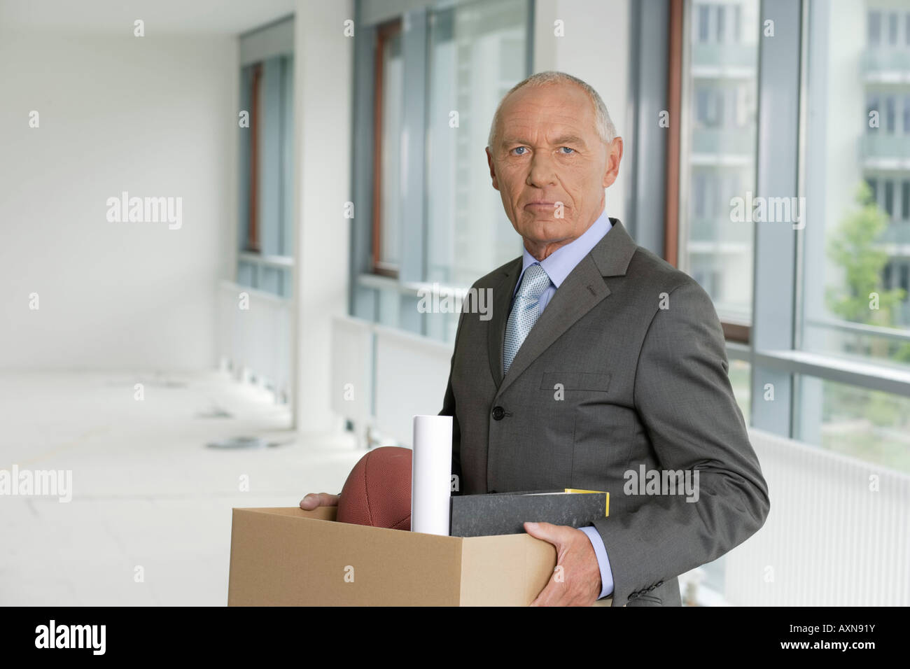Elderly manager carrying a cardboard box, standing in an empty office ...