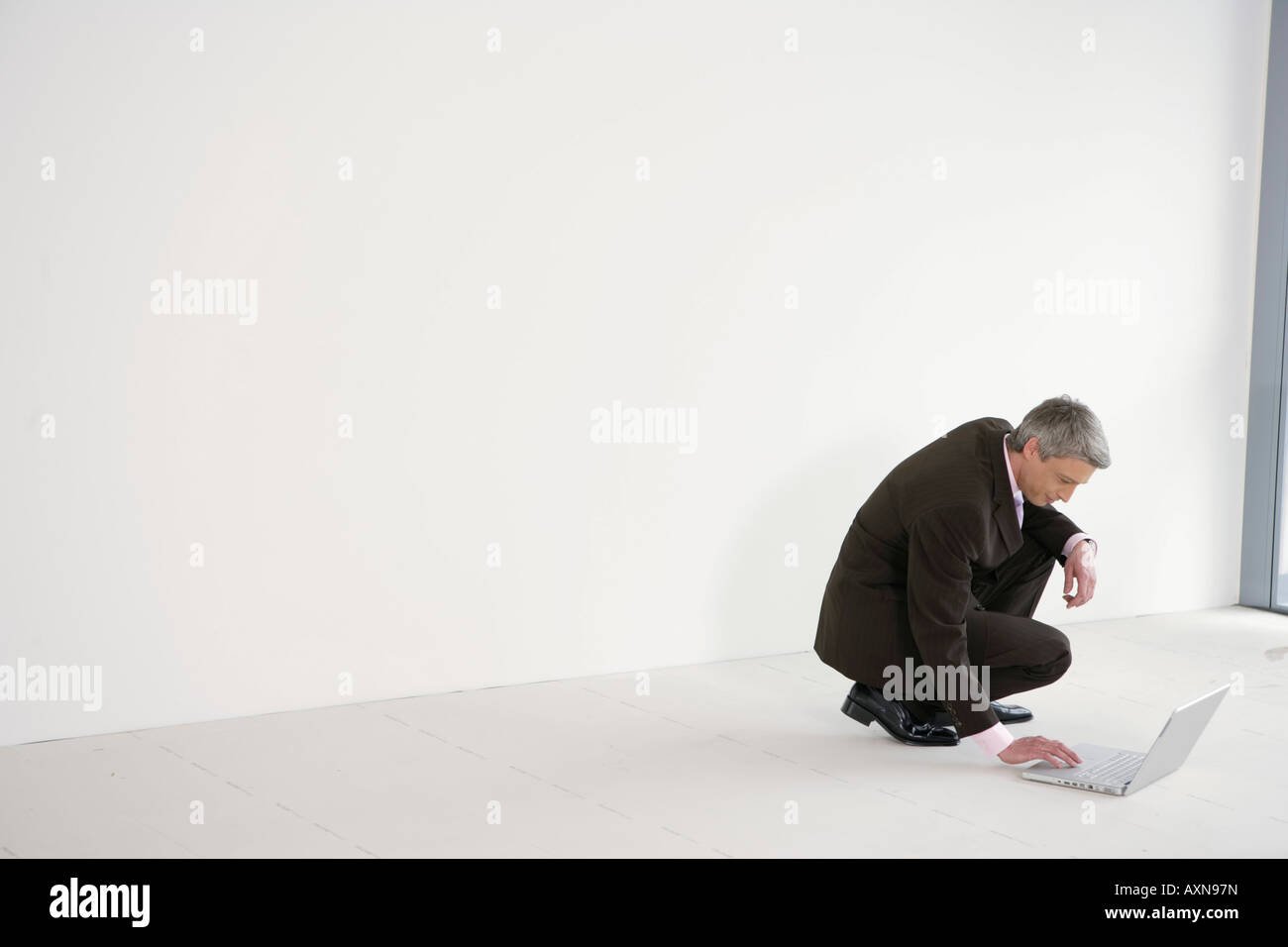 Businessman squatting on the floor working on laptop Stock Photo - Alamy