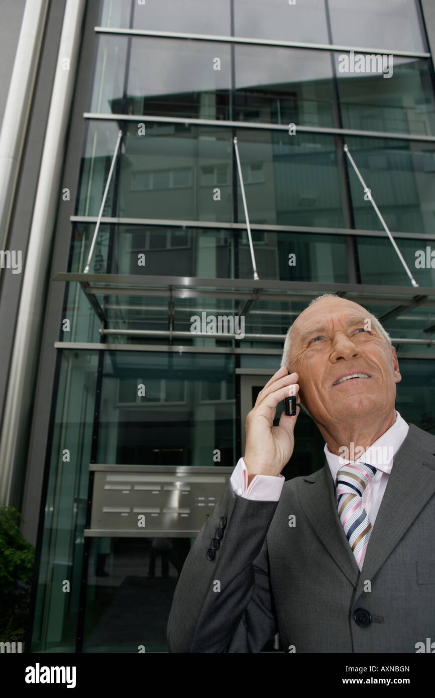 Elderly manager talking on his cell phone in front of office building ...