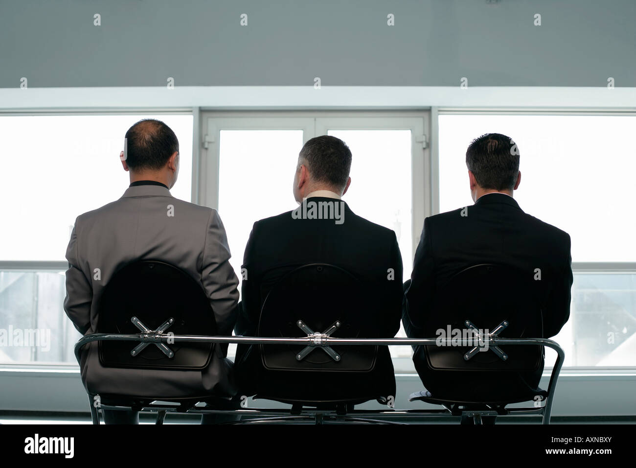 Three businessmen sitting on a bench looking down, rear view Stock ...